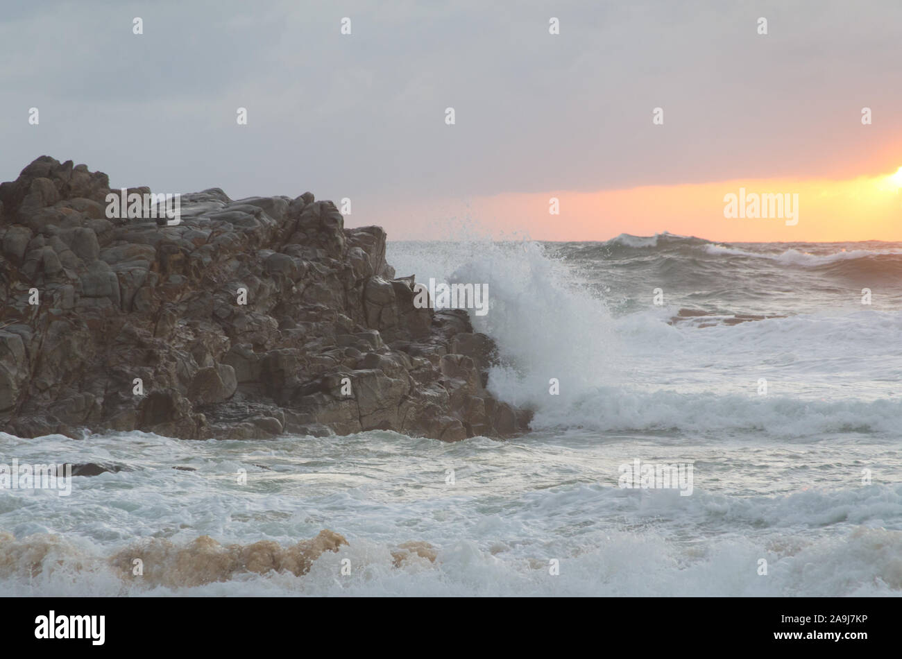 Sun rising over the horizon at a beach by a headland with waves ...