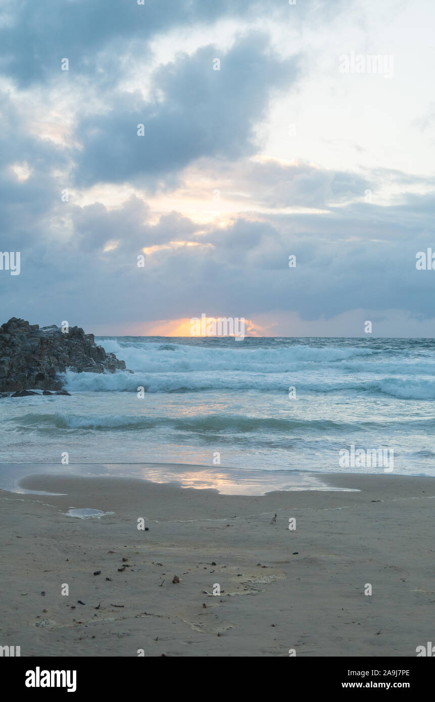 Sun rising over the horizon at a beach by a headland with waves ...
