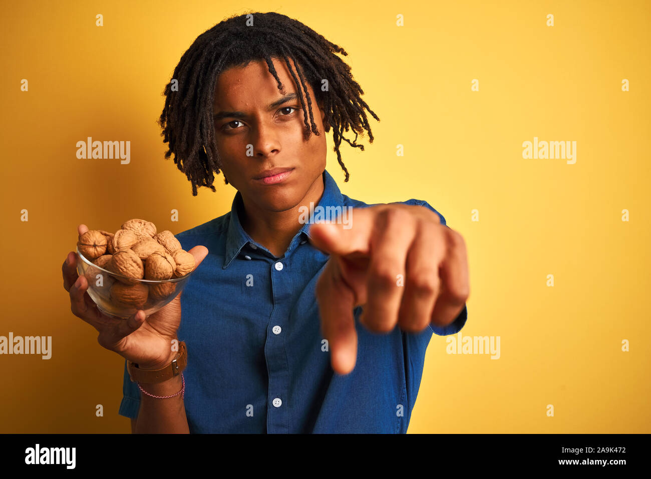 Afro american man with dreadlocks eating walnuts over isolated yellow ...