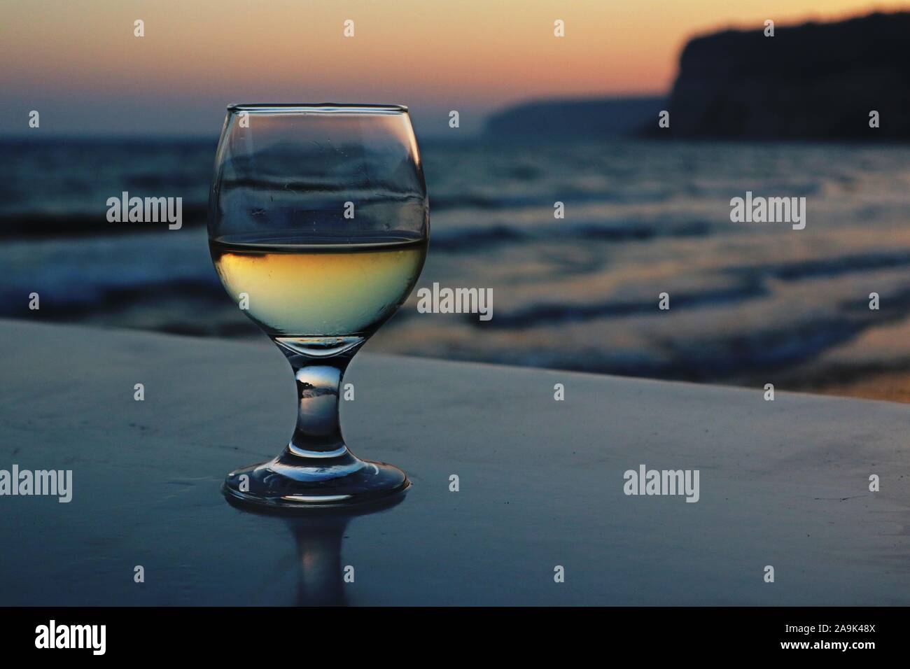Glass of white Cyprus wine on shiny surface against Mediterranean sea ...