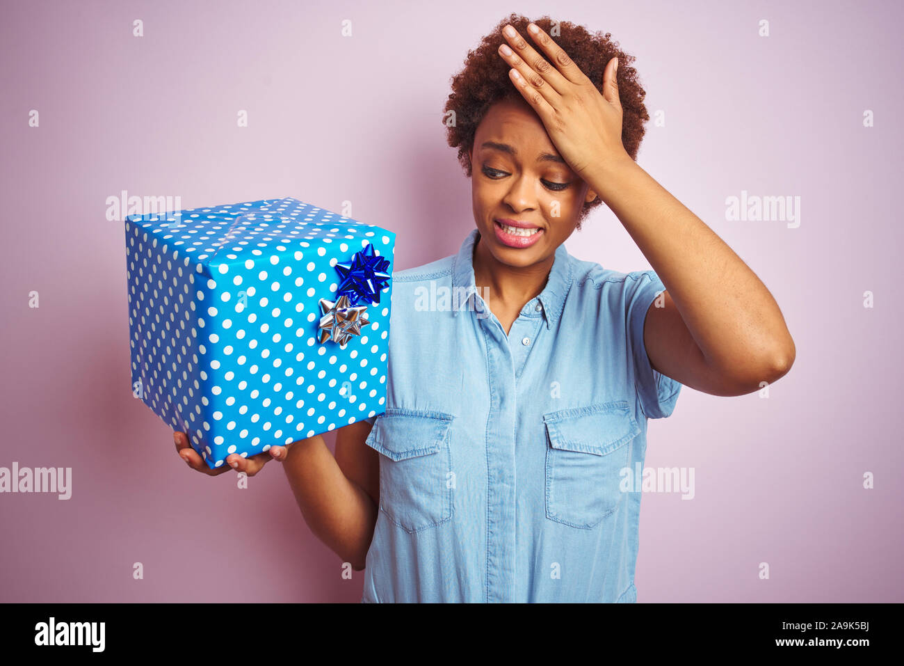 African american woman holding birthday gift over pink isolated ...