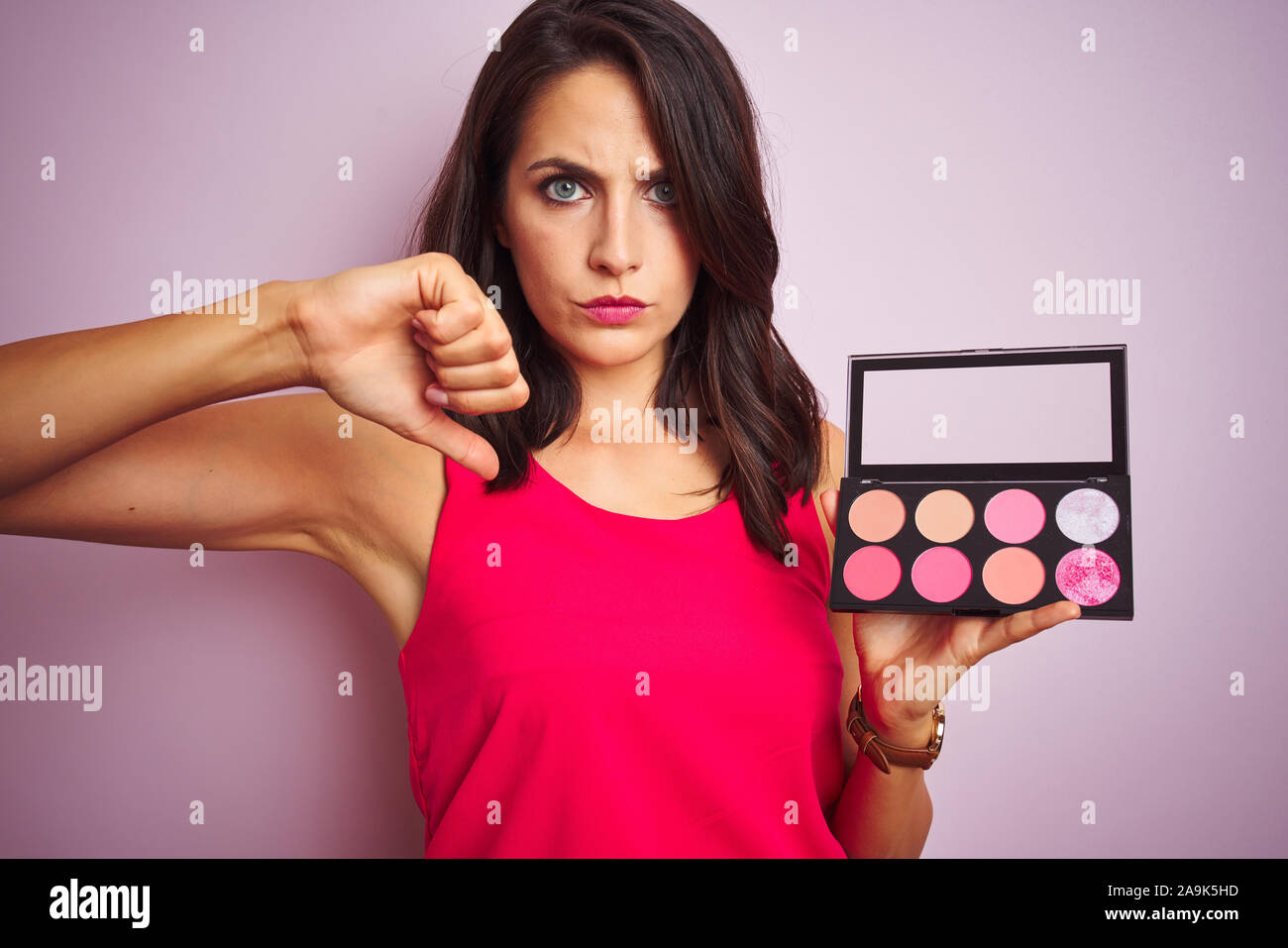 Young beautiful woman applying make up over pink isolated background ...