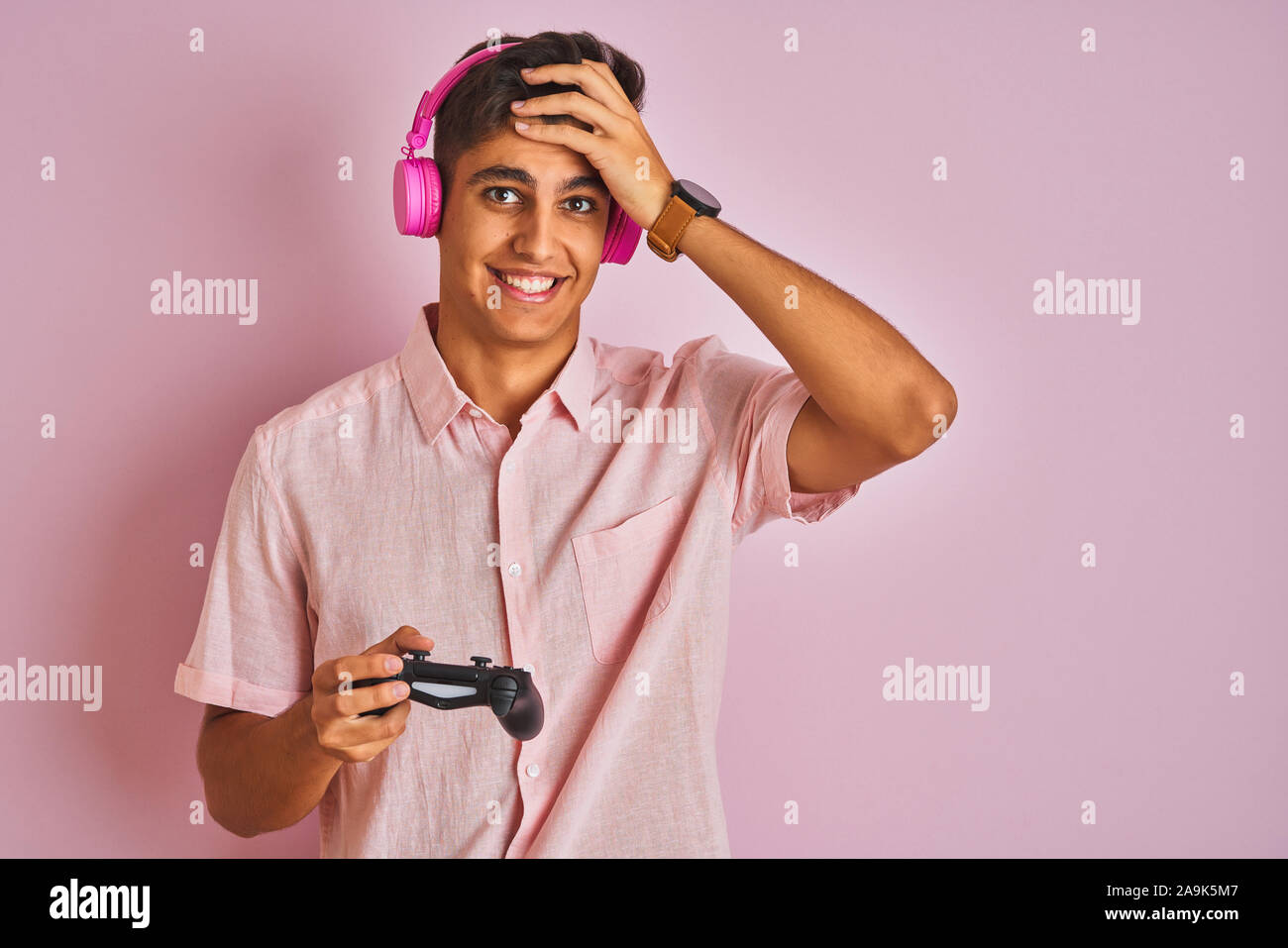 Indian gamer man playing video game using headphones over isolated pink ...