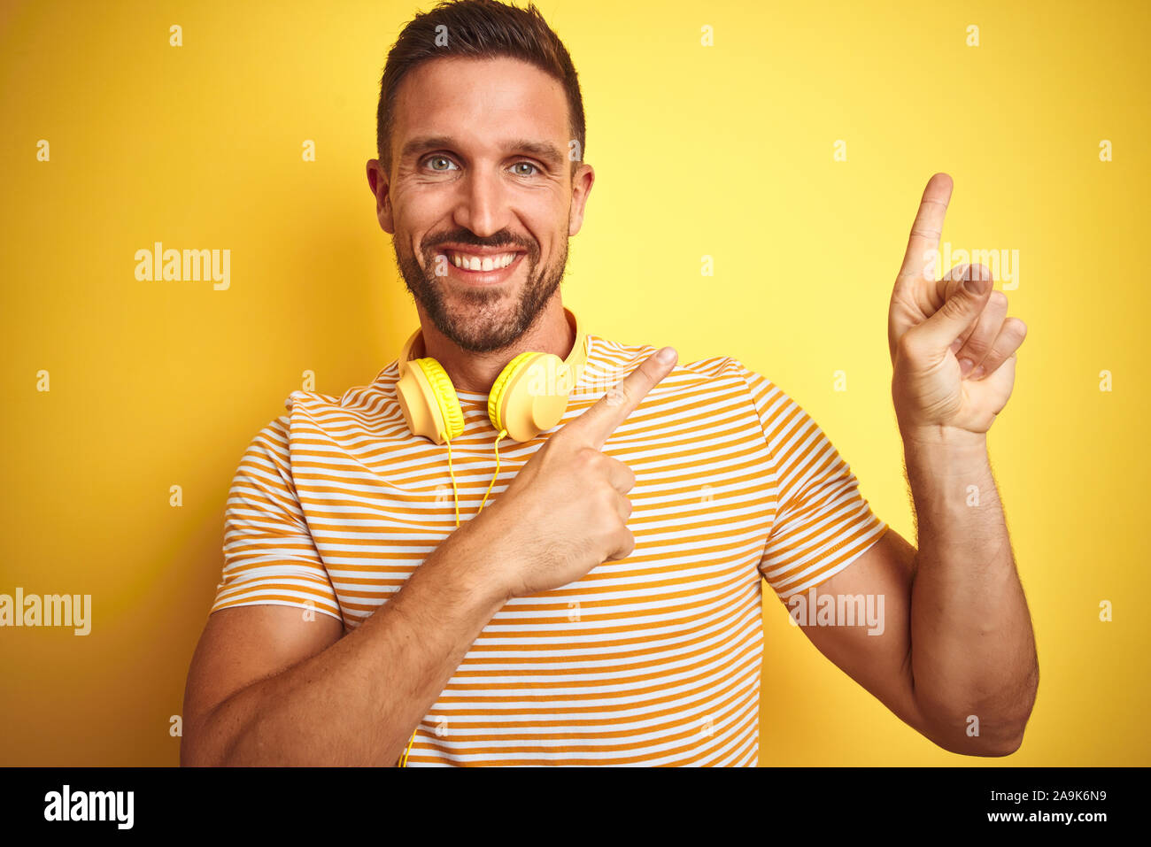 Young handsome man wearing headphones listening to music over yellow isolated background smiling ...