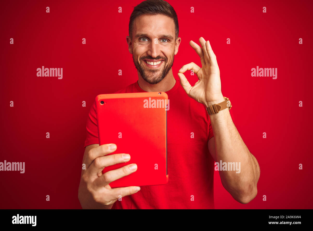 Young man using digital touchpad tablet over red isolated background ...