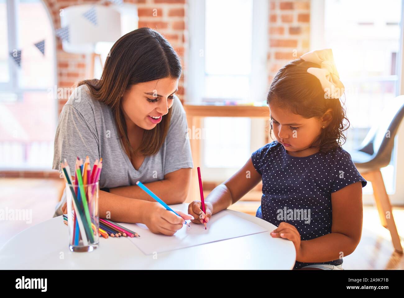 Beautiful teacher and toddler girl drawing draw using colored pencils ...