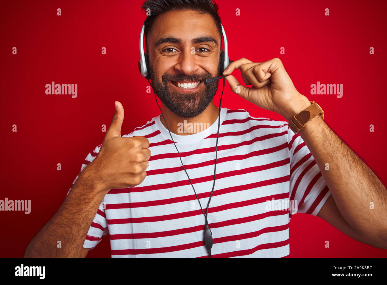Young indian call center agent man using headset over isolated red ...