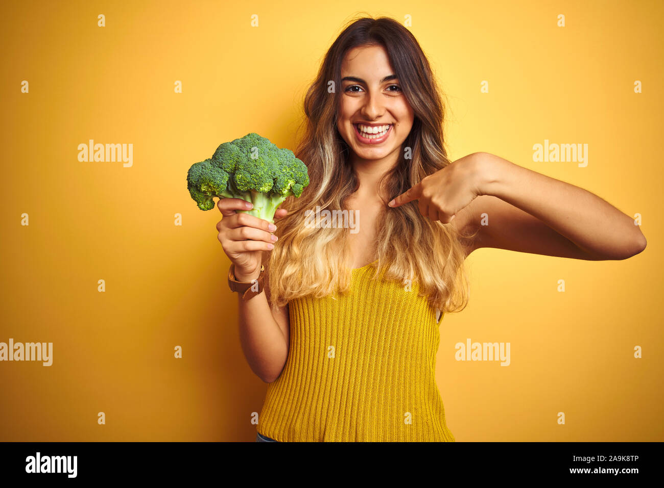 Young beautiful woman eating broccoli over yellow isolated background ...