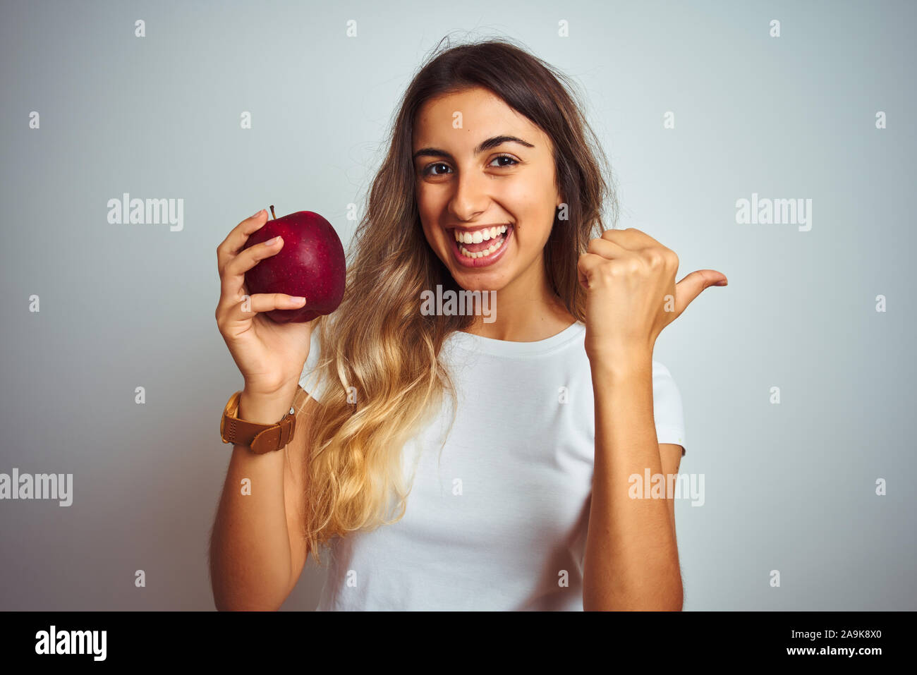 Young beautiful woman eating red apple over grey isolated background ...