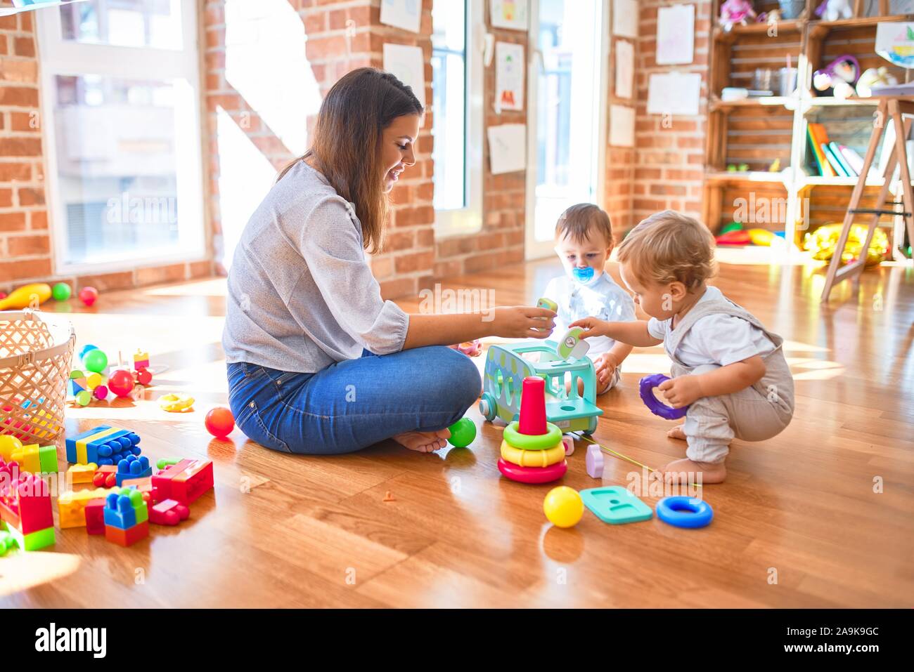 Beautiful teacher and toddlers playing around lots of toys at ...