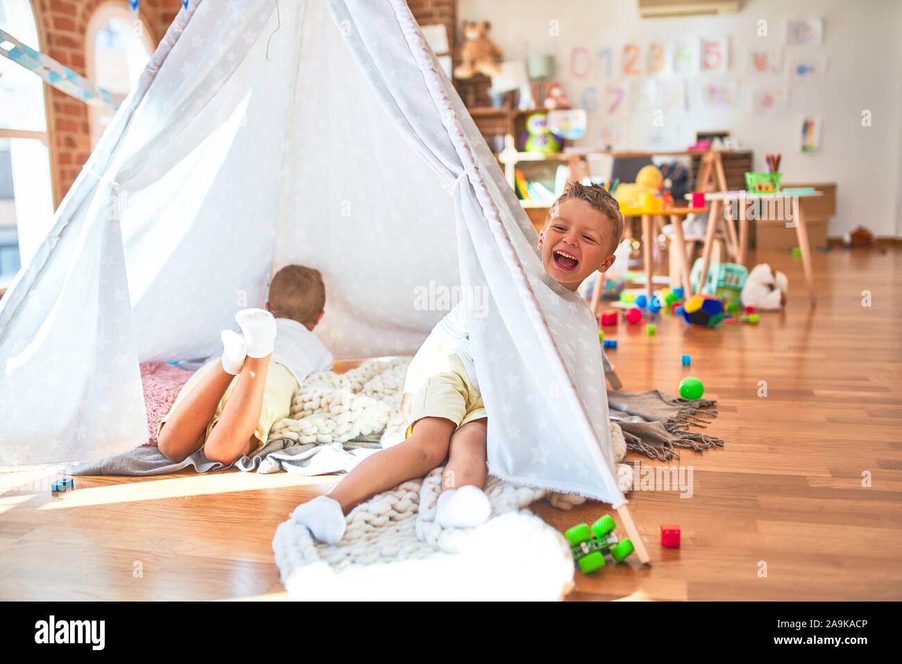 Adorable blonde twins playing inside tipi around lots of toys at ...
