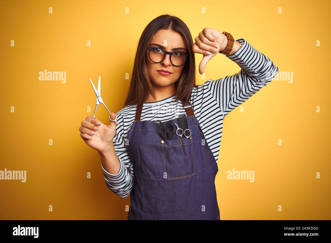 Young beautiful hairdresser woman holding scissors standing over ...