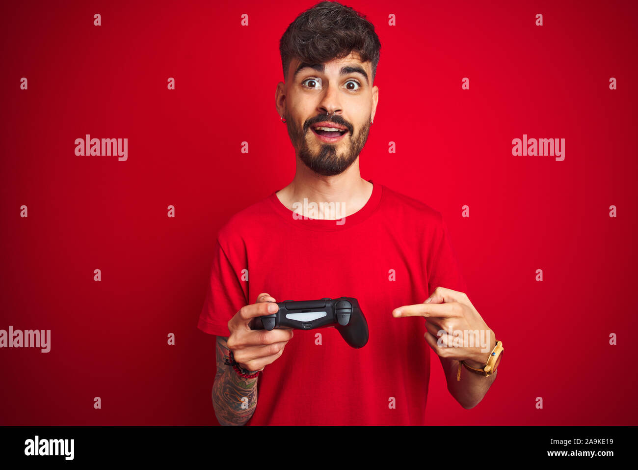 Young gamer man with tattoo playing video game standing over isolated ...