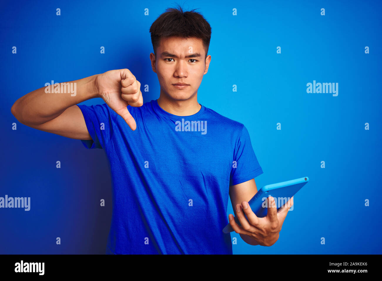 Young asian chinese man using tablet standing over isolated blue ...