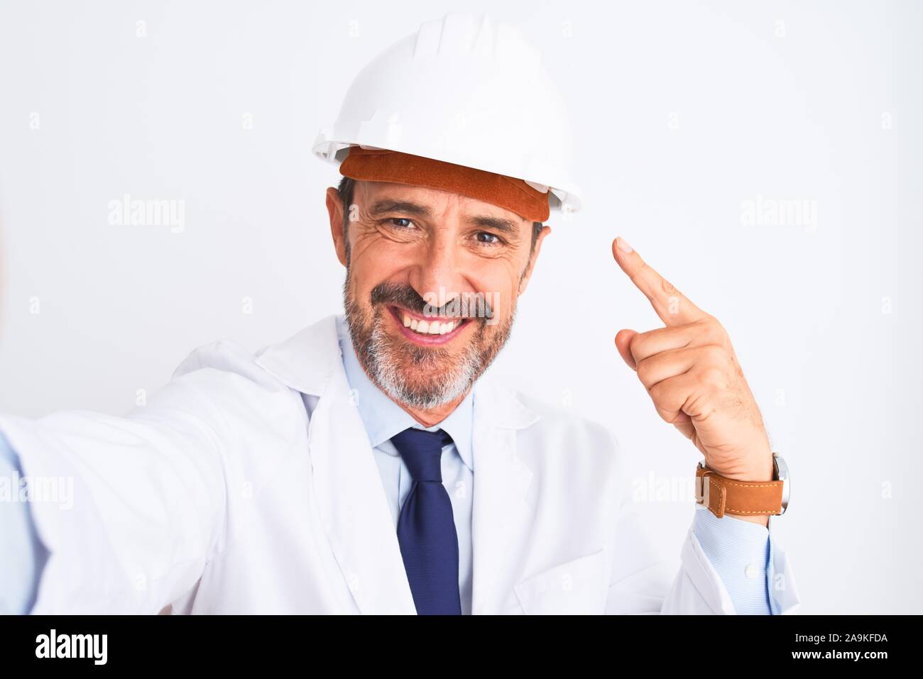 Middle age engineer man wearing helmet make selfie over isolated white ...
