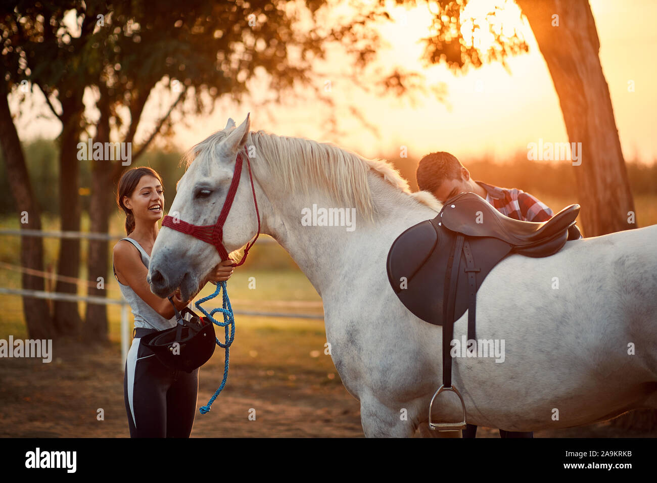 A man mounting saddle on the horse while young woman holds it Stock ...