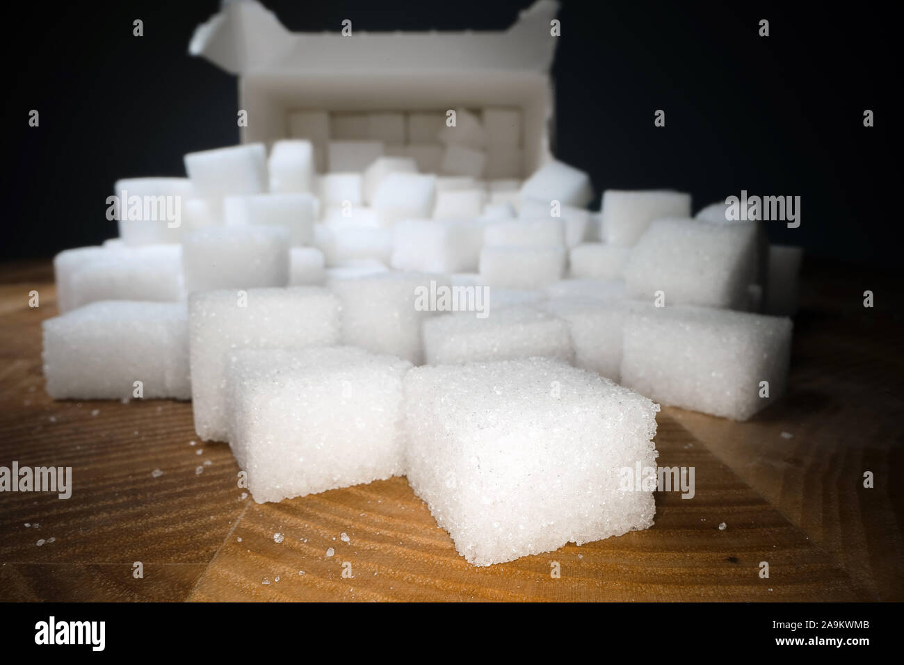 Macro shot of sugar cubes next to carton box on wooden table. Unhealthy ...