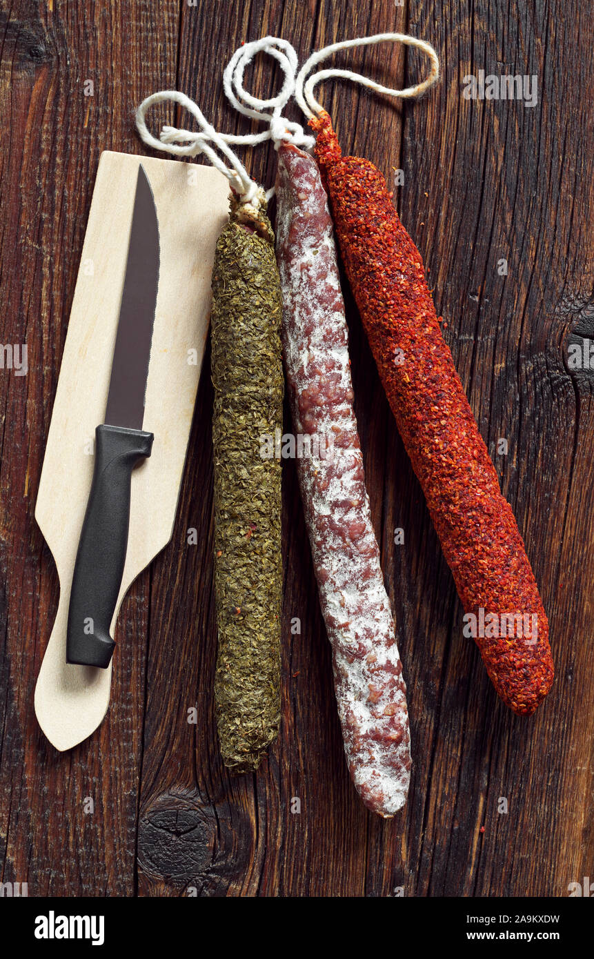 Three various salami sausages, cutting board and knife on dark wooden ...