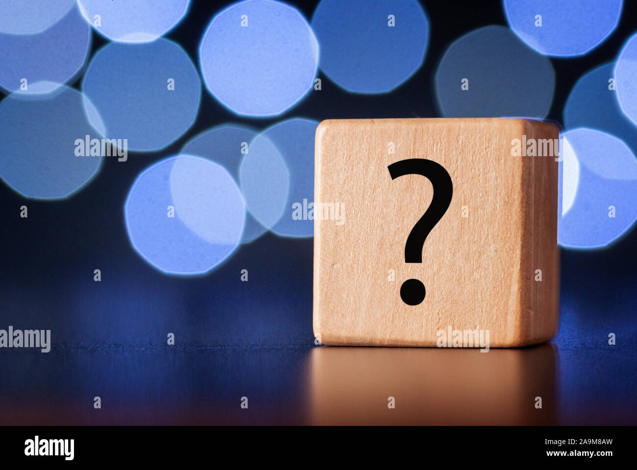 Wooden cube with question mark on a reflective table with background of ...