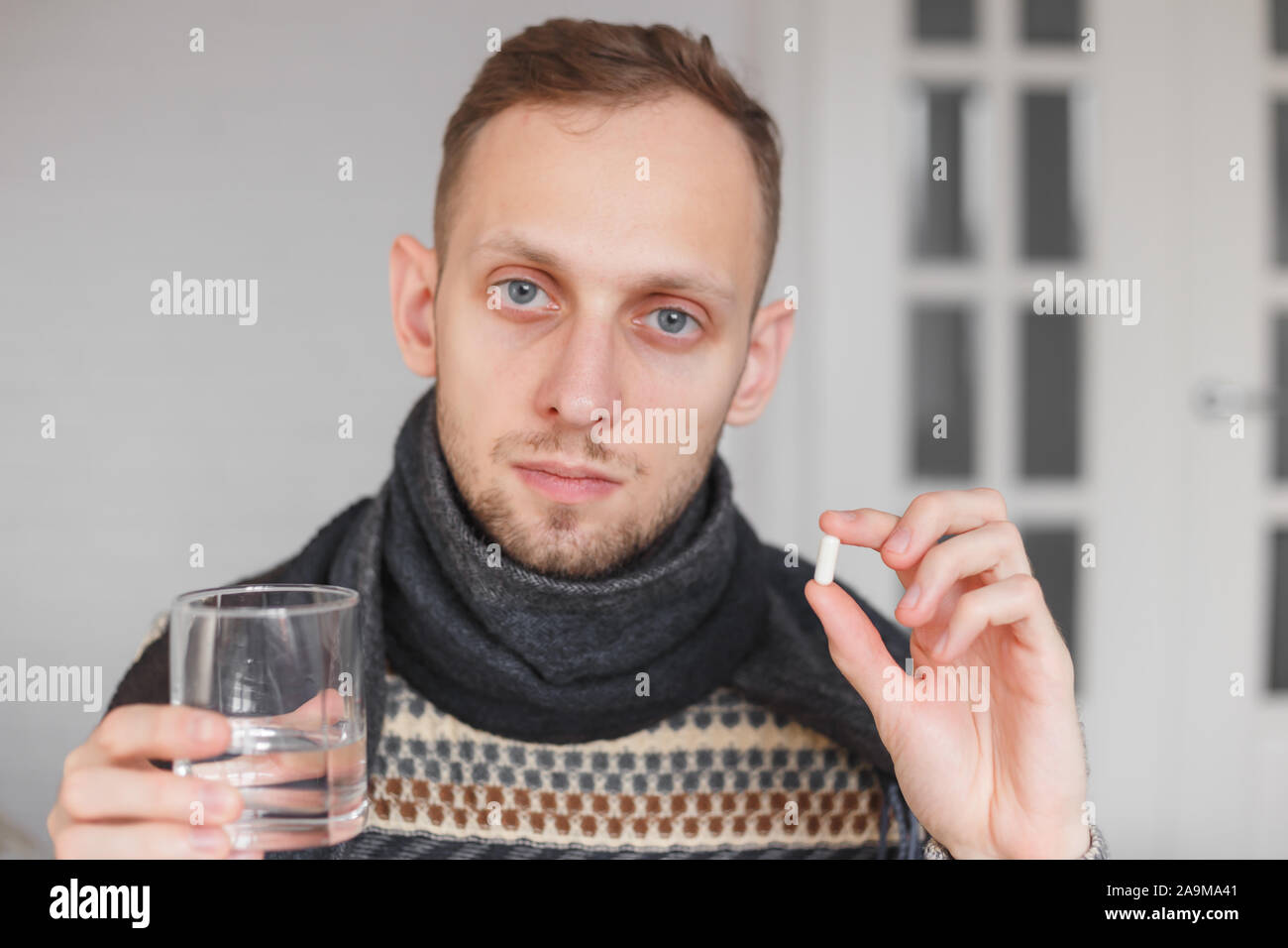 Young man has the flu. Holding antibiotic capsule and a glass of water ...