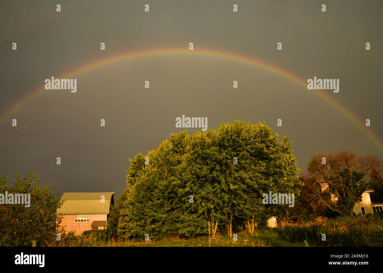 Rainbow arching over a farmstead in the country during the summer, with ...