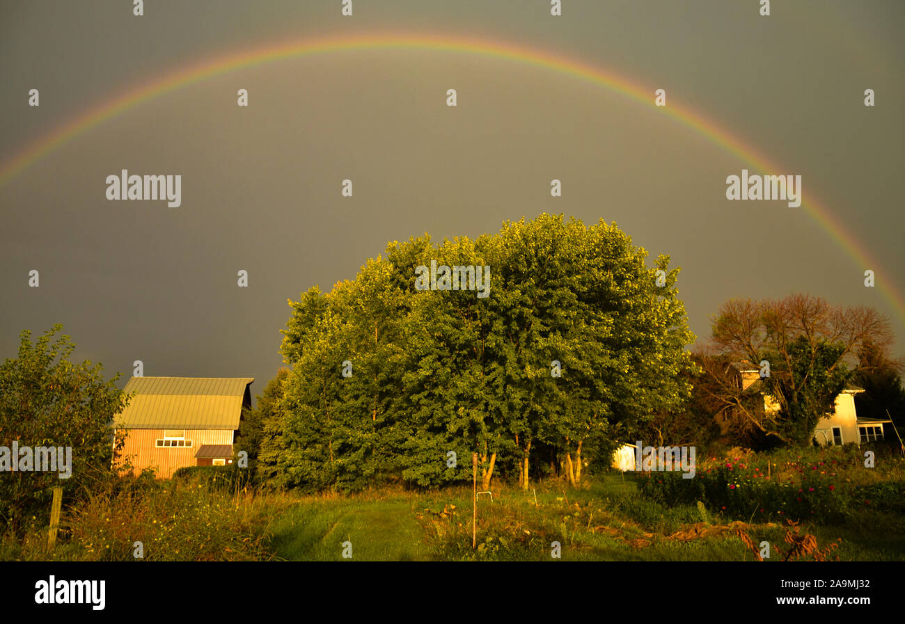 Rainbow arching over a farmstead in the country during the summer, with ...