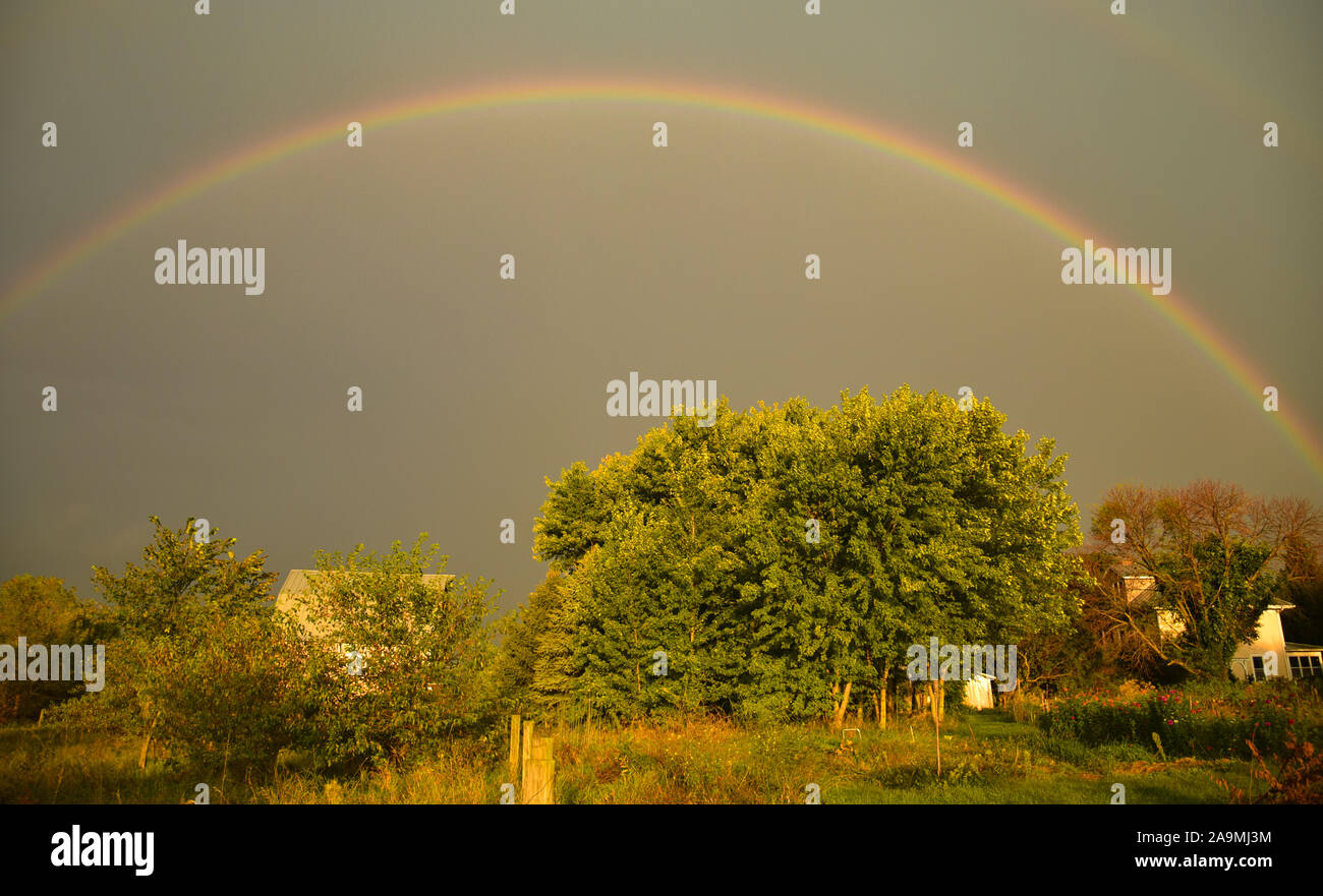 Rainbow arching over a farmstead in the country during the summer, with ...