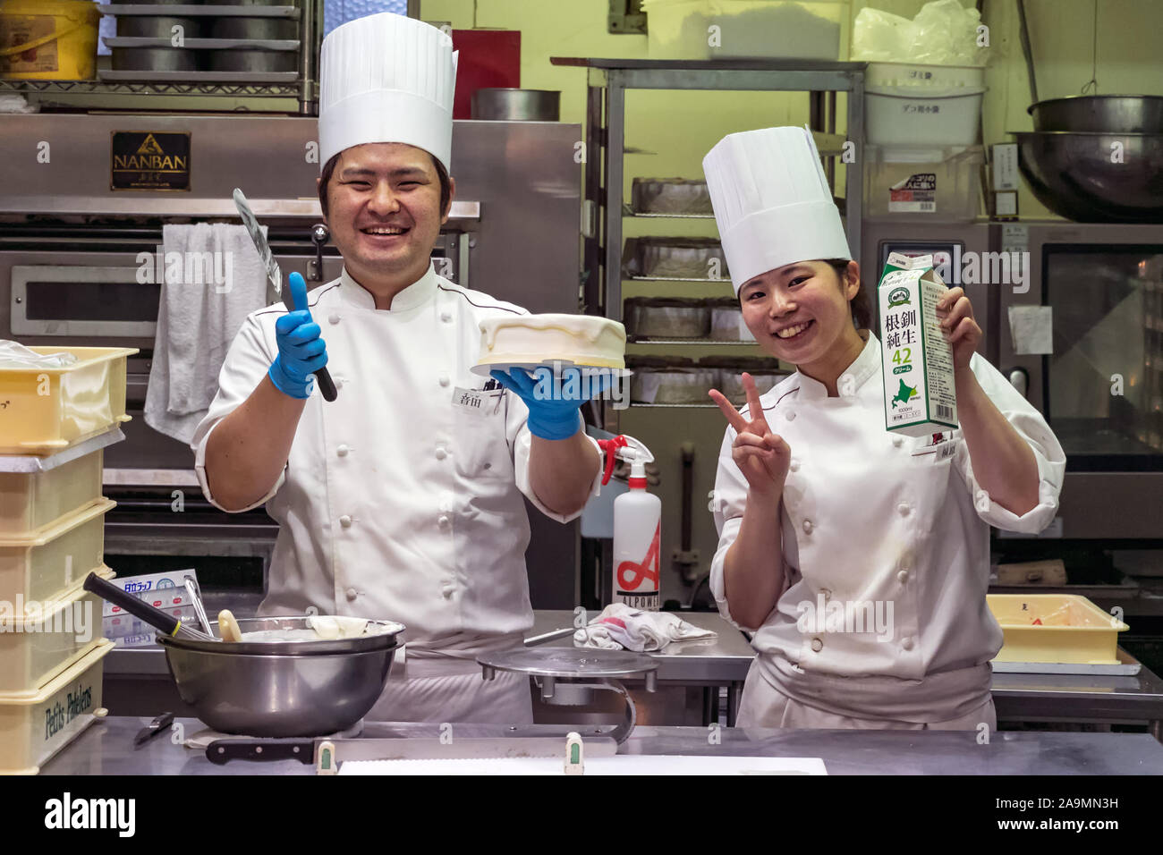 Two Japanese pastry chefs smiling holding a round cake to decorate at ...