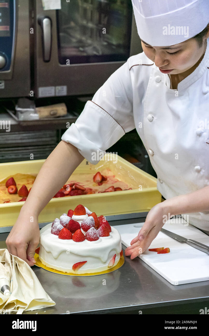A Japanese female pastry chef showing a cake decorated with cream and ...