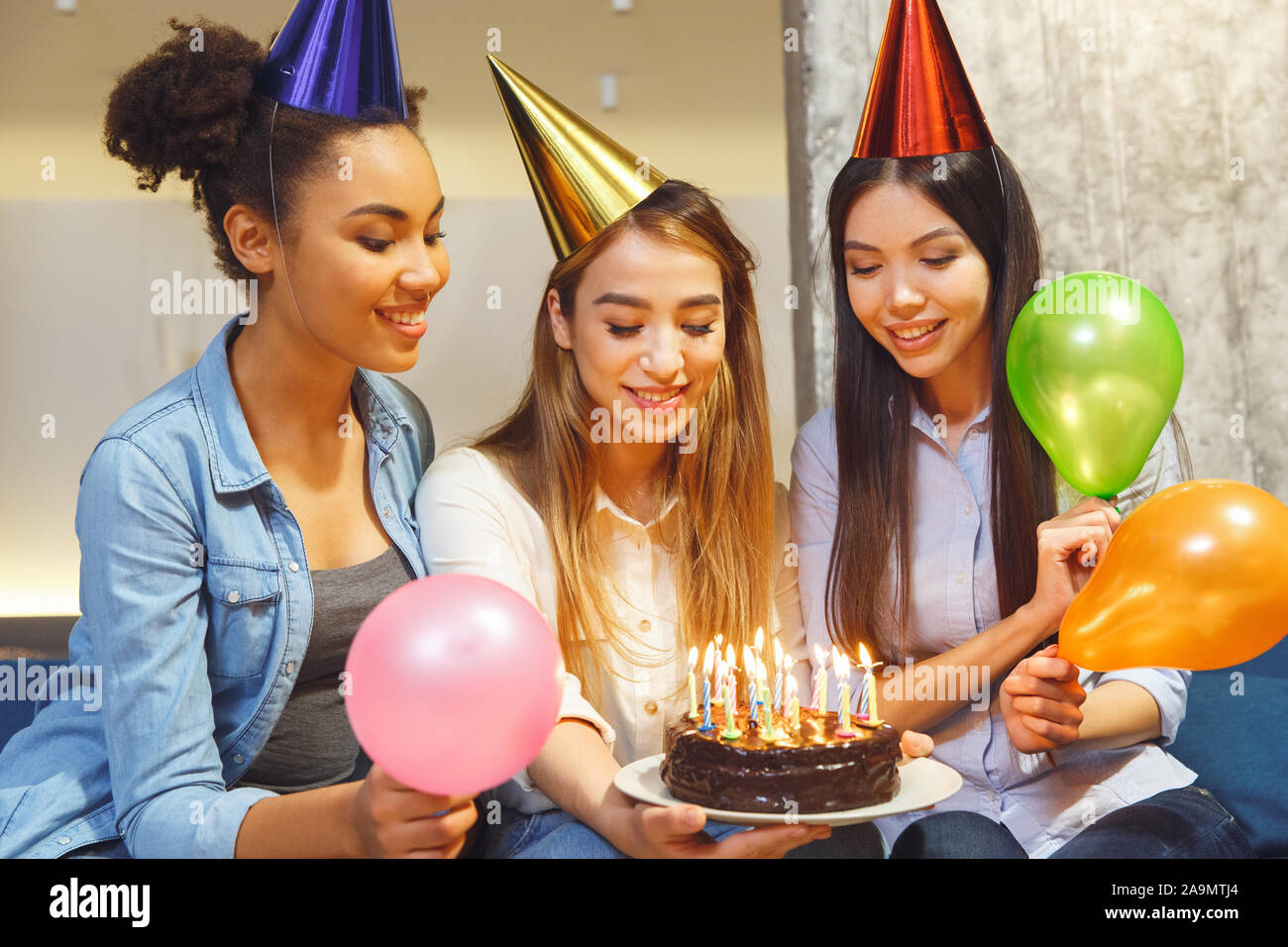 Group of friends having party indoors fun together ready to make a wish ...