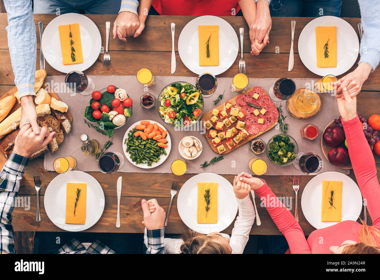 People sitting at home behind table, praying together before dinner ...