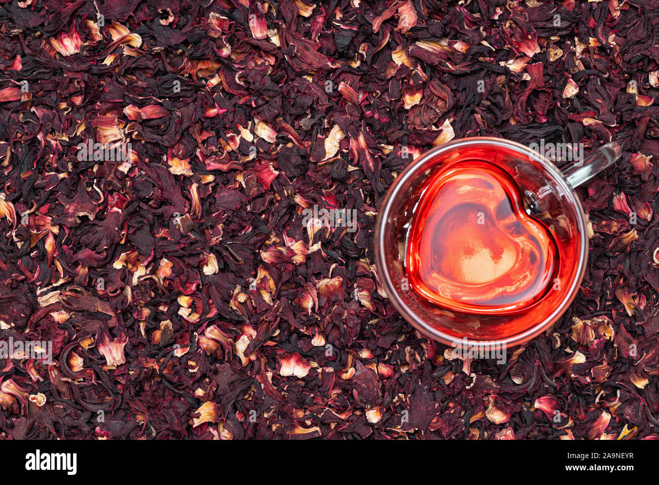 top view of red hibiscus tea in glass heart shaped cup on dry rose ...