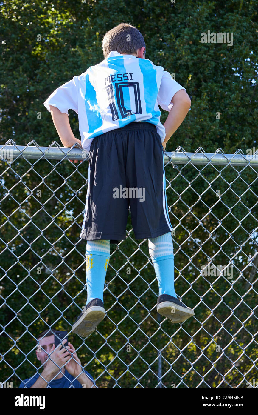 Young boy wearing Messi jersey no. 10 and climbing a chain link metal ...