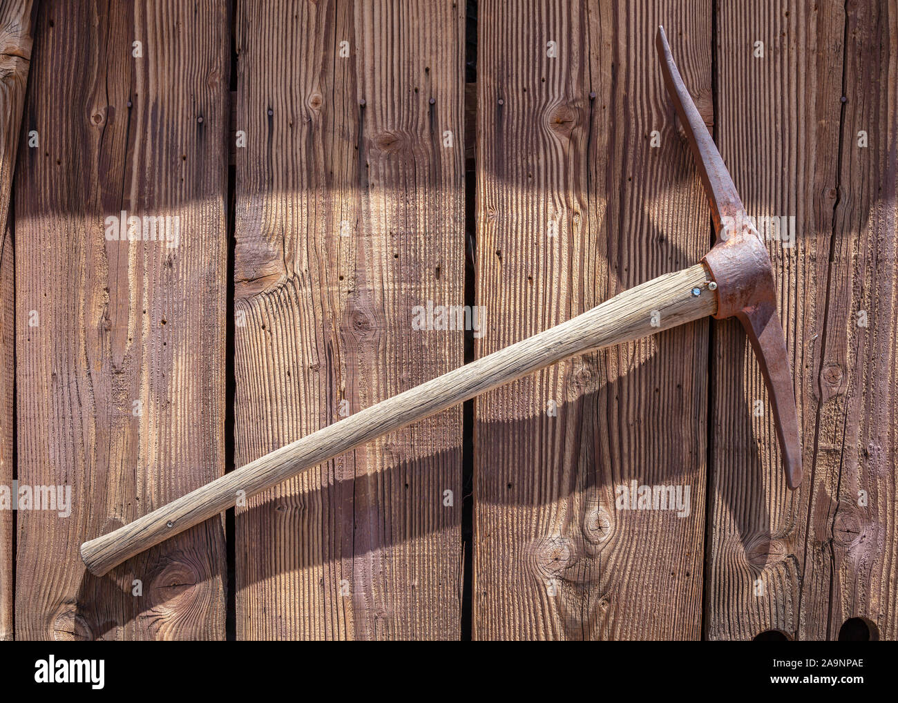 Rusty pick mattock hanging on a wooden wall, sunny spring day in Calico ...