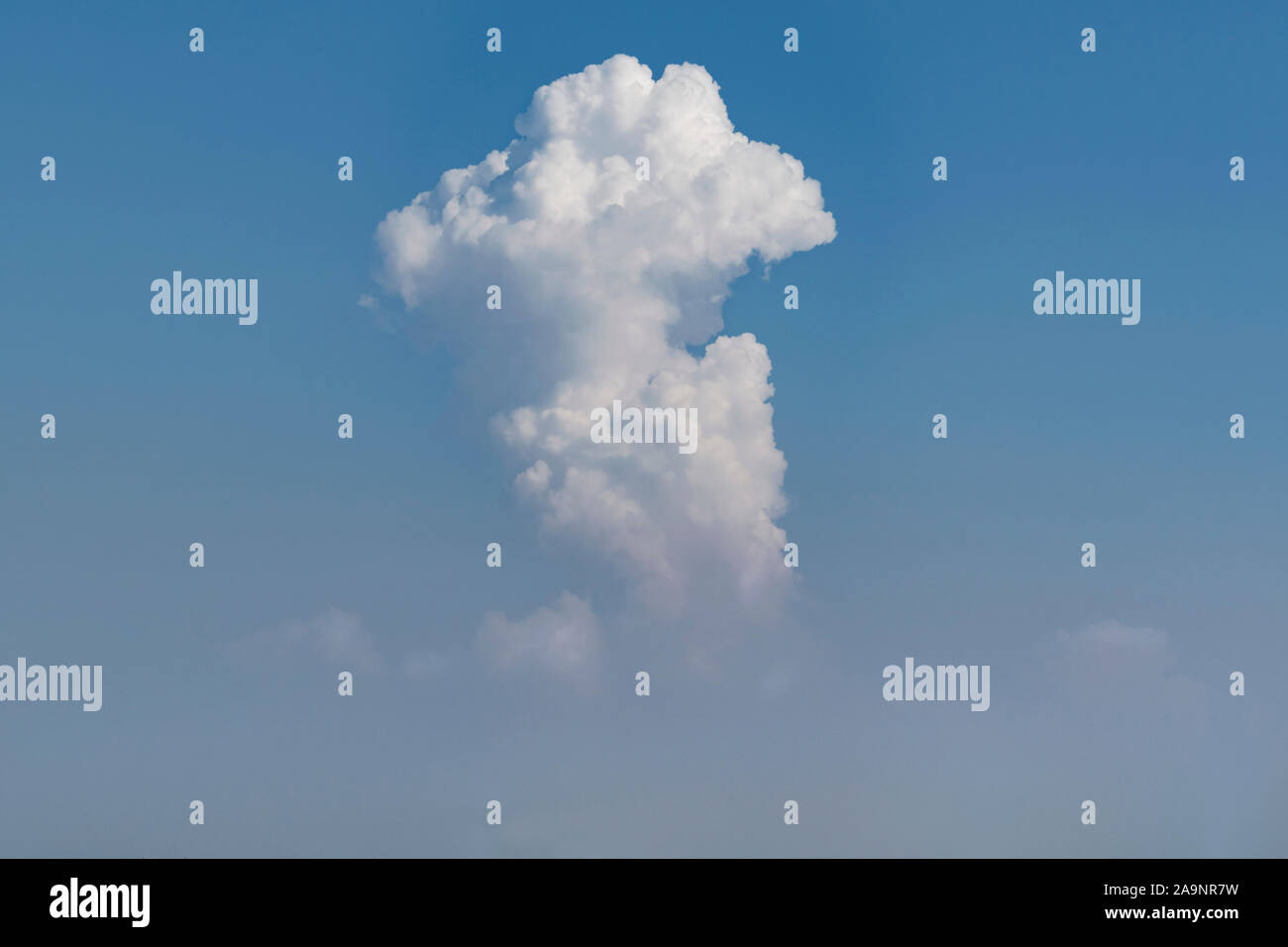 dramatic white cumulous thunder cloud rising in a column above the haze ...