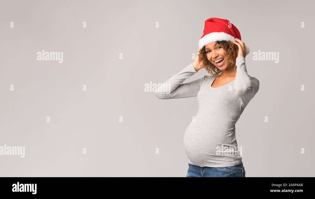 Excited pregnant woman in Santa hat posing over grey background Stock ...