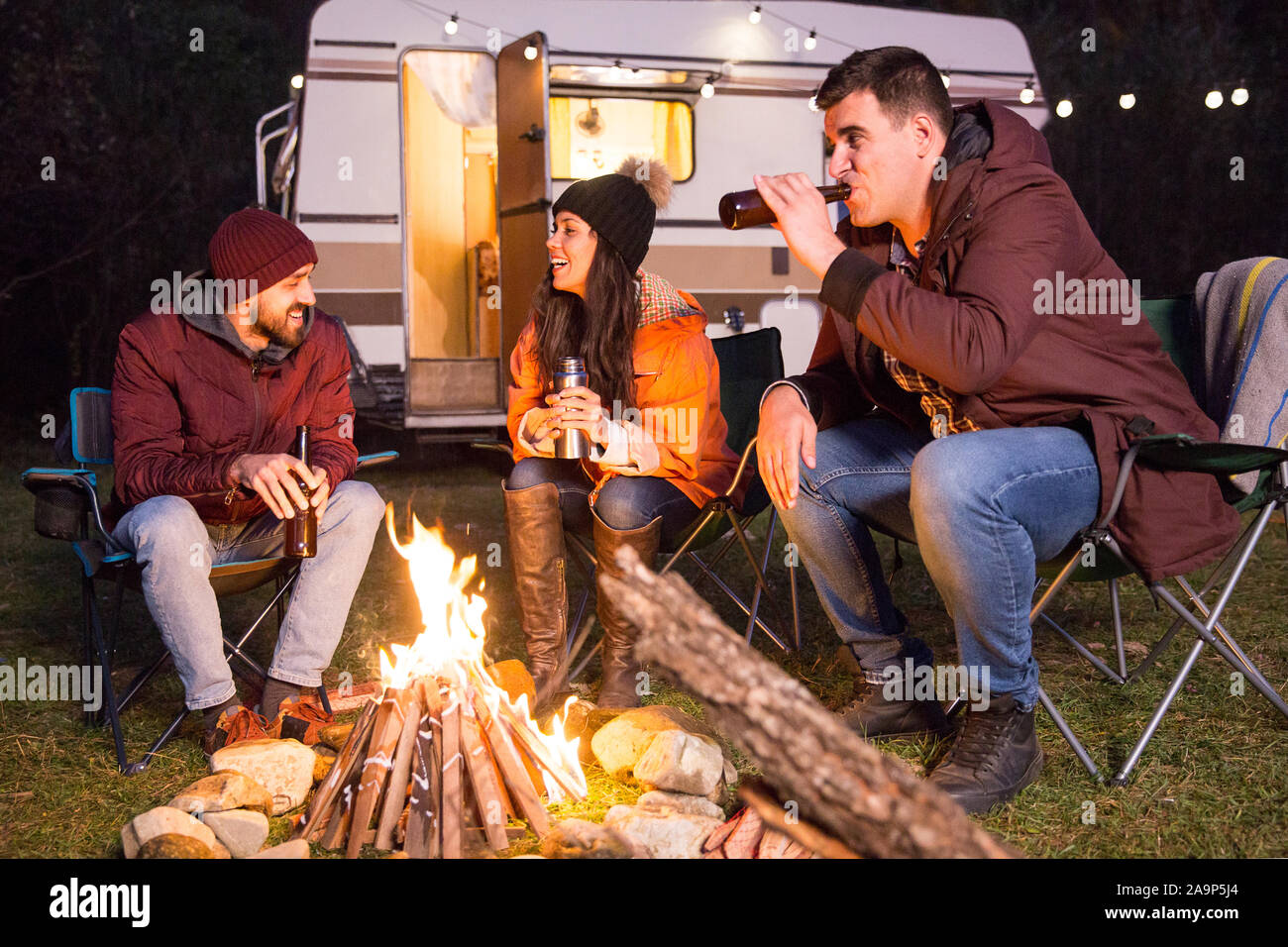 Cheerful friends laughing and drinking beer in a camp site around camp ...