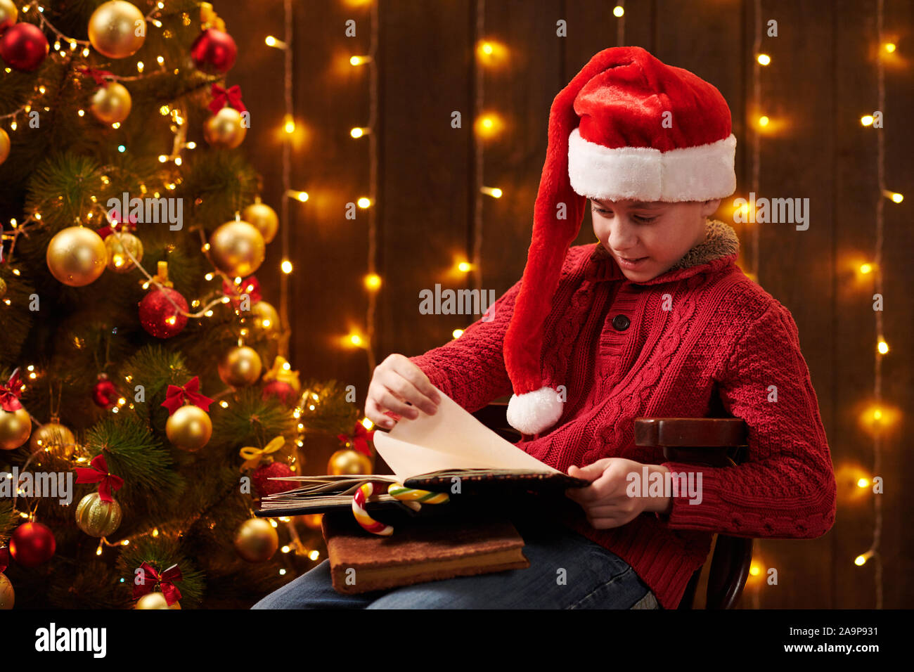 Teen boy reading book, sitting indoor near decorated xmas tree with ...