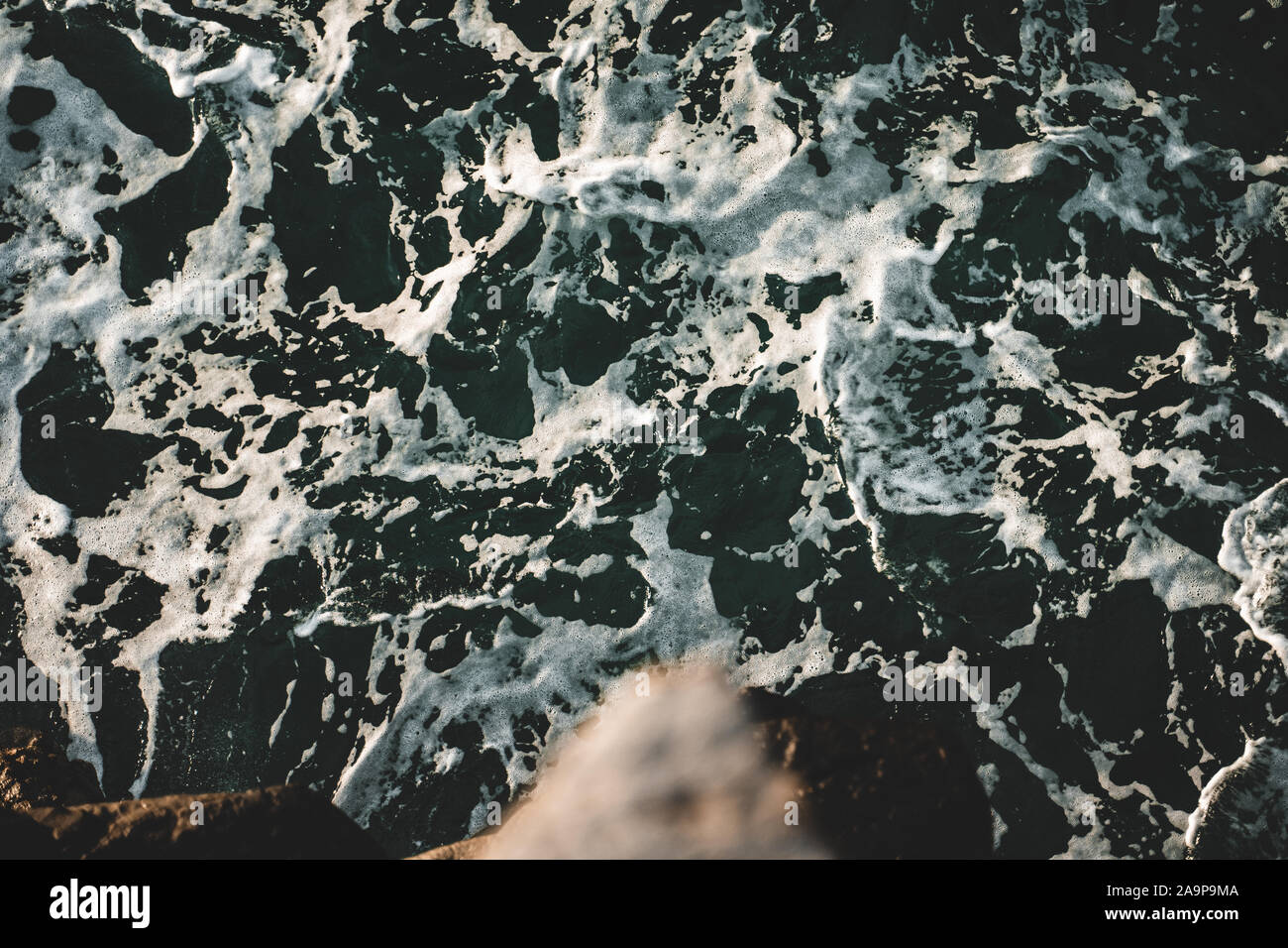 Looking over the cliffs edge to the dark ocean water with whitewash on ...