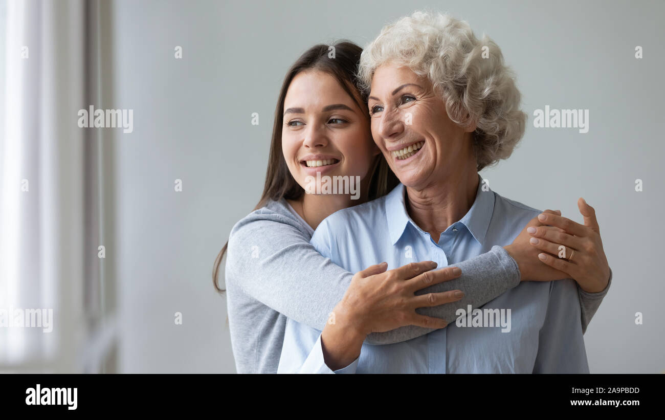 Happy young granddaughter embrace smiling old grandma look through ...