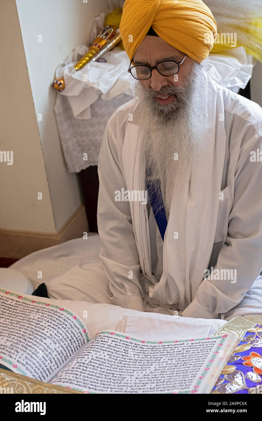 A Sikh priest in a turban reads from the Guru Granth Sahib holy book at ...