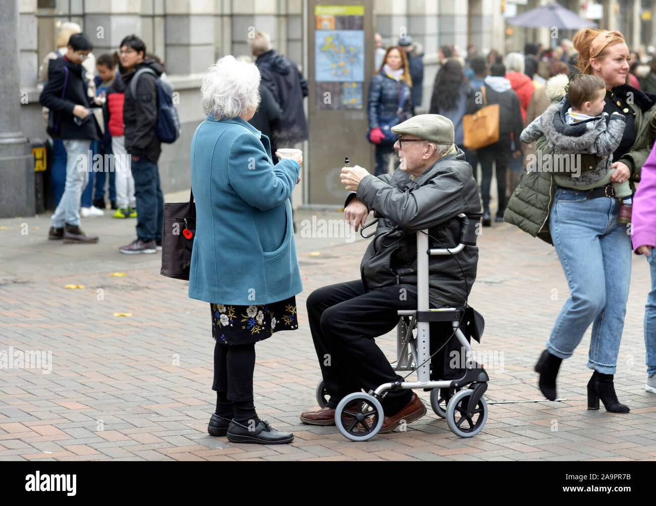 Old couple, man seated on mobility cart, in among crowd Stock Photo - Alamy