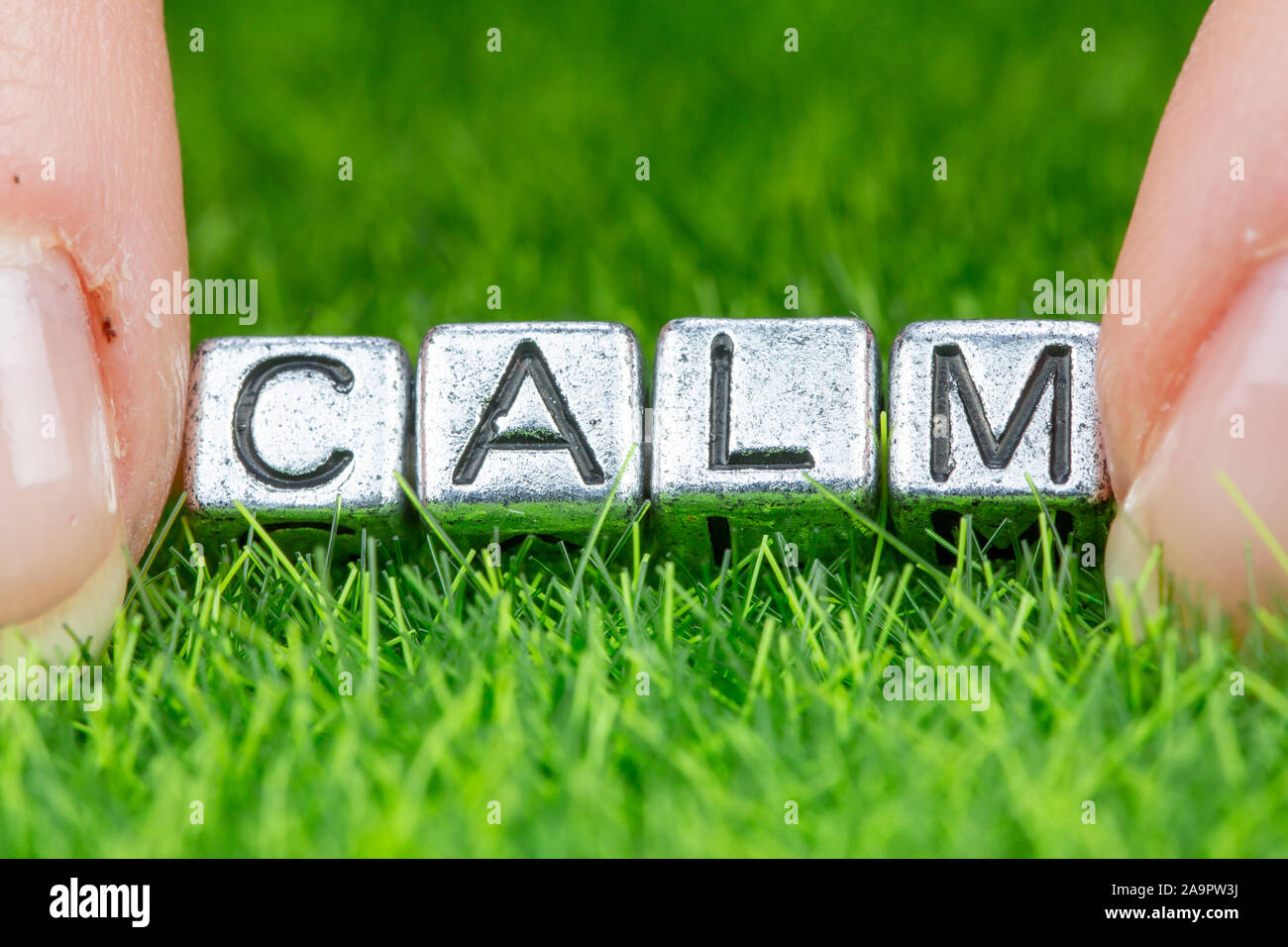Close up on word CALM written in metal letters laid on grass and held ...