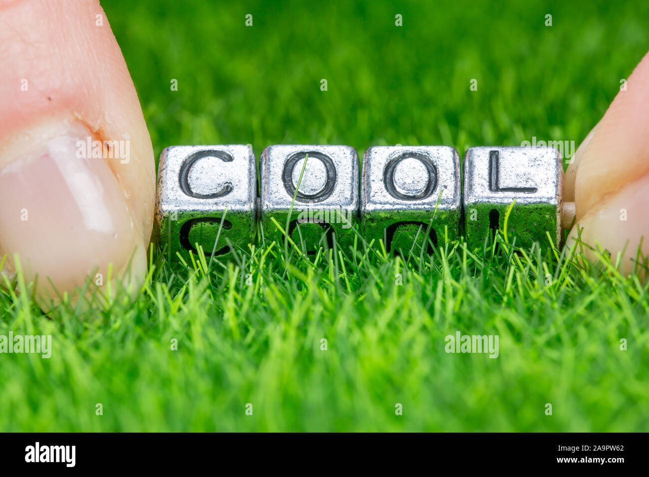 Close up on word COOL written in metal letters laid on grass and held ...