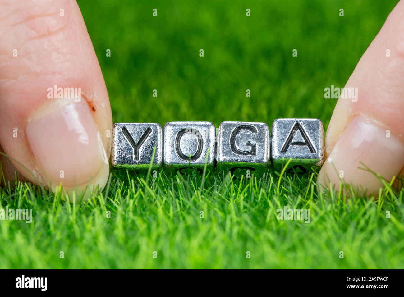 Close up on word YOGA written in metal letters laid on grass and held ...