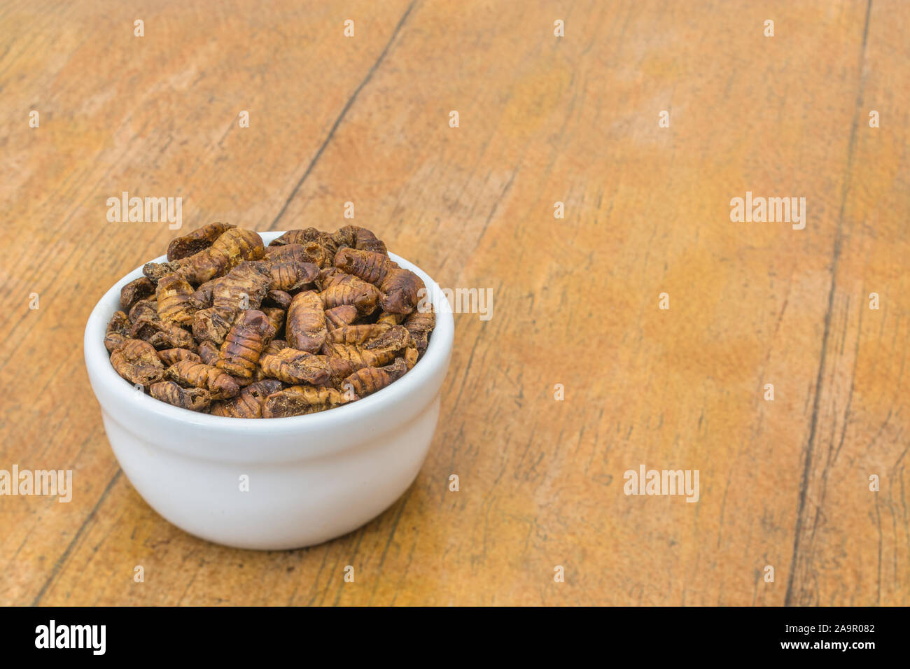 Dishes of edible insects. Silkworm pupae / Bombyx mori on faux wood ...