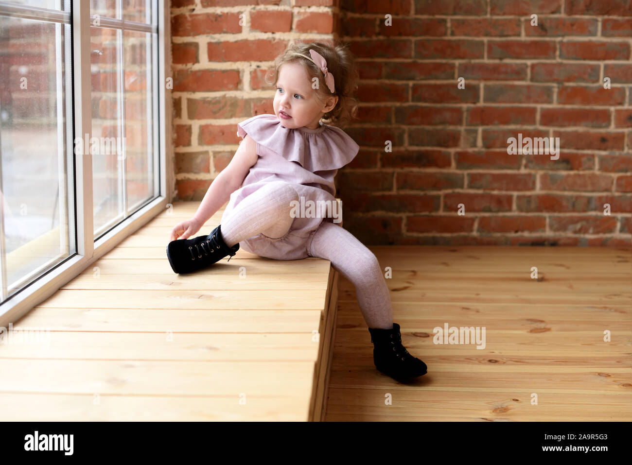 Little kid concept. Adorable toddler girl at window sill alone in empty ...