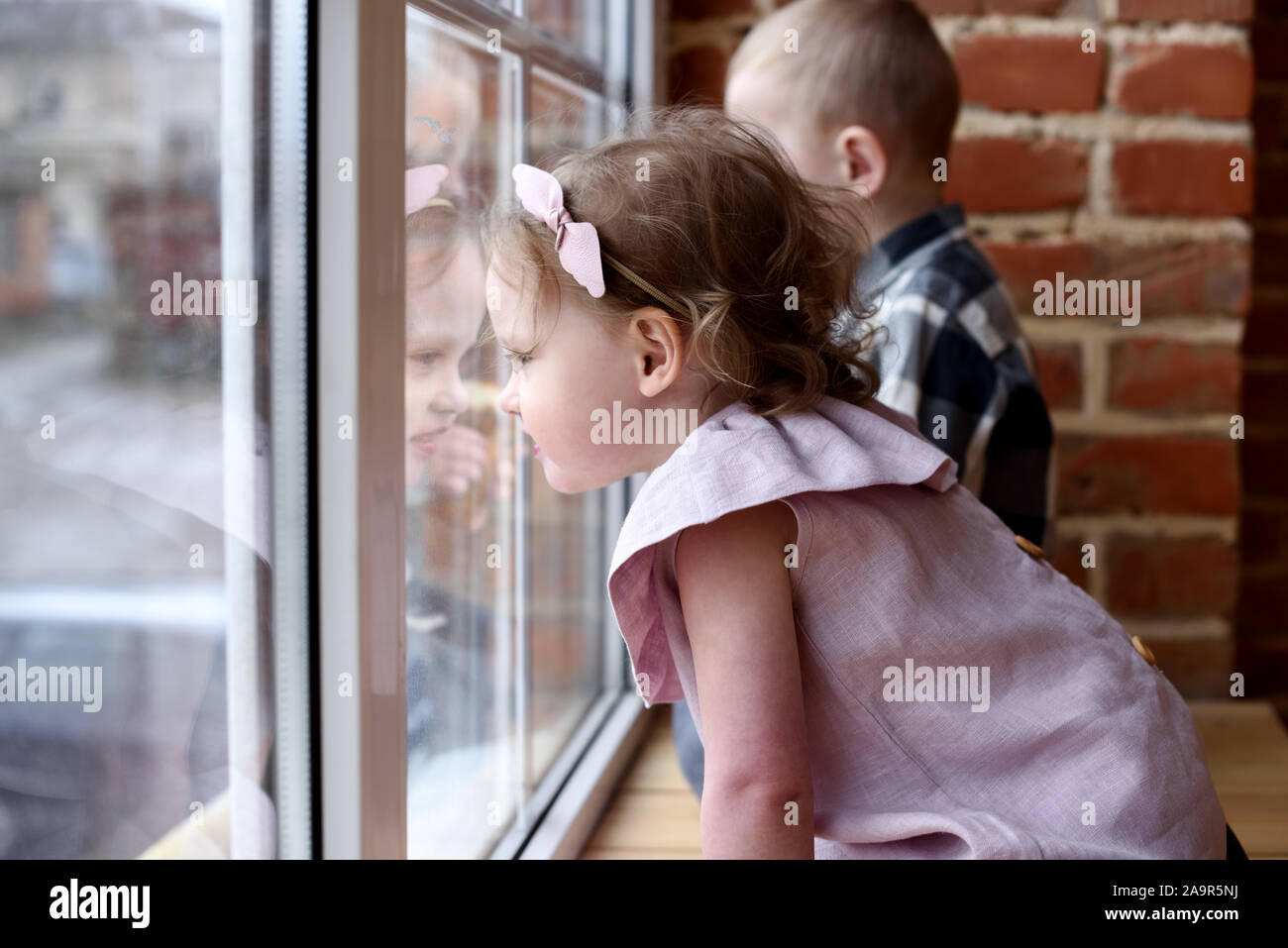 Children or siblings concept. Little girl and boy sitting at window and ...