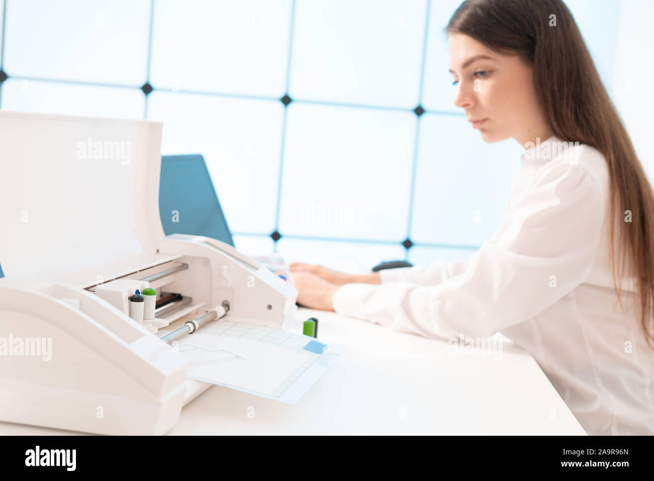 Young woman in the office of the printing company sets up a plotter for ...