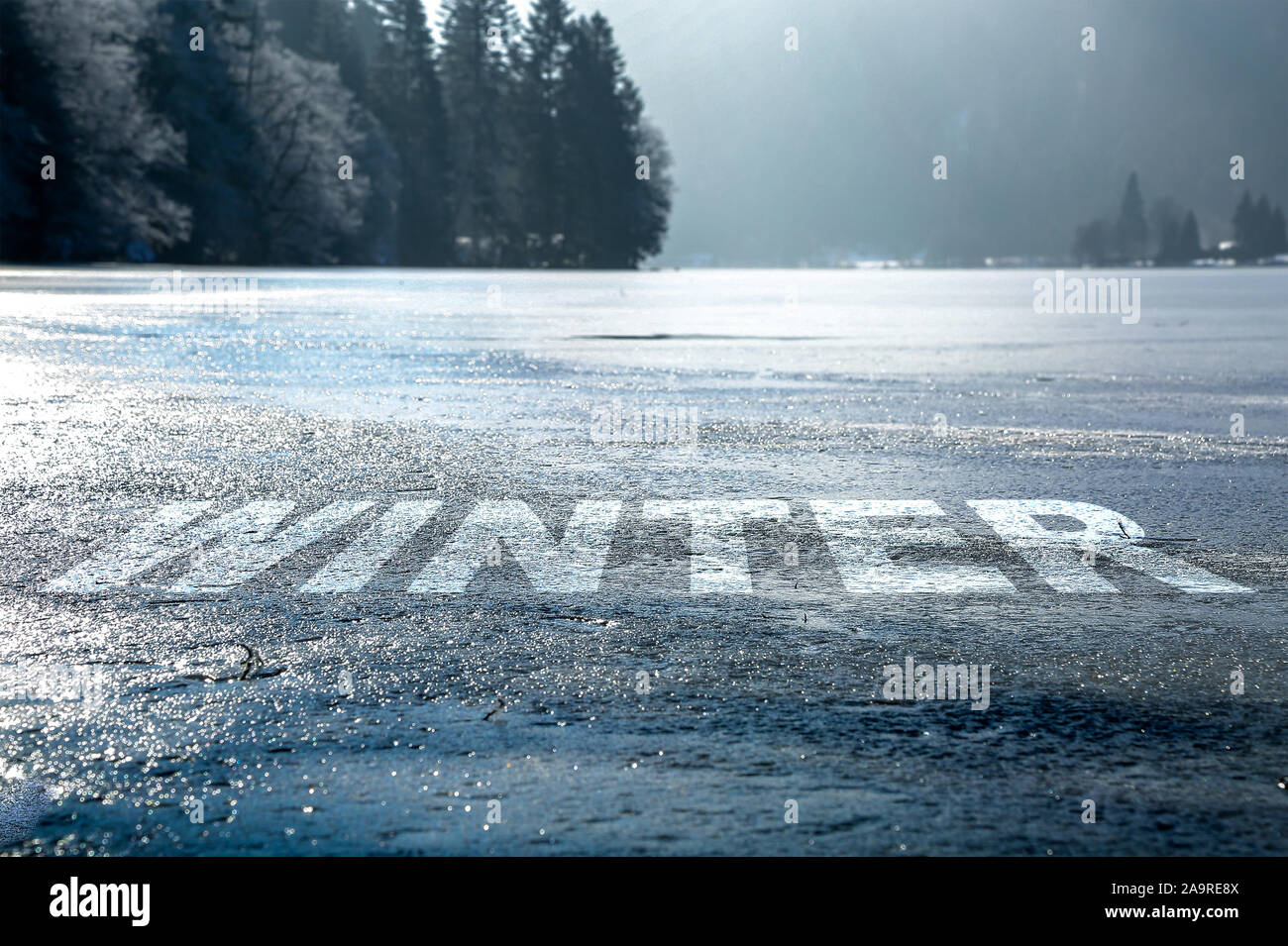 word winter inscribed on the frozen ground of a lake with snowy ...